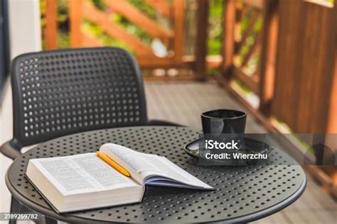 나무 울타리와 녹색 환경이 있는 발코니에 서 있는 검은 커피 컵이 있는 플라스틱 정원 테이블에 노란색 펜으로 성경을 엽니다 0명에 대한 스톡 사진 및 기타 이미지 Istock