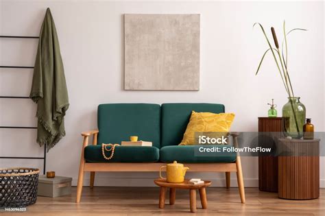 모의 포스터 병 녹색 소파 우아한 나무 스탠드 식물 상자 말린 꽃과 개인 액세서리가 있는 유리 꽃병이 있는 거실의 고전적인 공간 베이지 색 벽 가정 장식 템플렛 장식함에