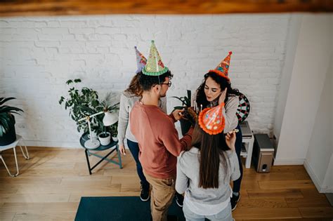 생일 여성을 놀라게하고 촛불이 켜진 케이크를 들고 파티 모자를 쓰고 웃는 젊은 친구들 20 24세에 대한 스톡 사진 및 기타 이미지 20 24세 25 29세 가정