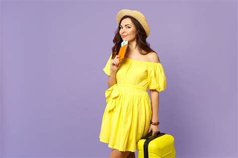 노란 드레스에 웃는 젊은 여자 여름 모자 개최 가방 여권 탑승권 티켓 파스텔 바이올렛 벽 배경에 고립 사람들은 진심으로 감정