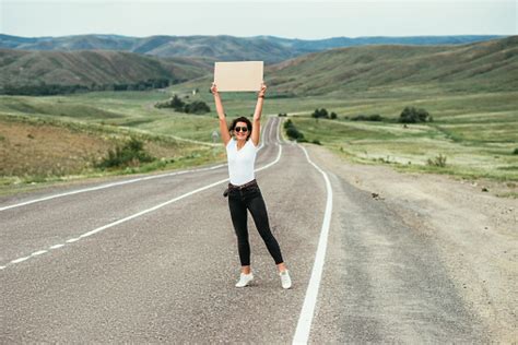 소녀는 히치하이크입니다 여행에 대한 열정 자동차 여행의 개념 히치하이크 여행 한 여성이 빈 골판지 표지판 모형으로 도로에서 차를 멈추려고 합니다 자동차로 여행 30 34세에