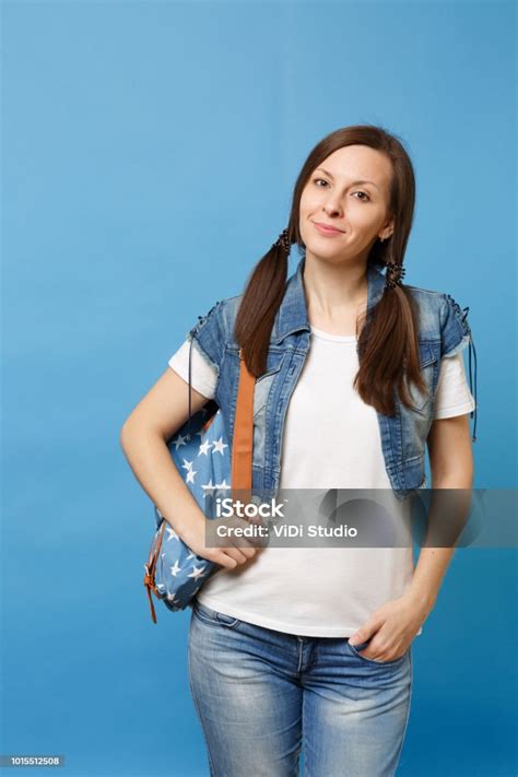 파란색 배경에 흰색 T셔츠와 데님 옷 주머니에 손을 유지 하는 배낭에 젊은 아름 다운 귀여운 여자 학생의 고립 대학에서 교육입니다 광고에 대 한 공간을 복사 합니다 20