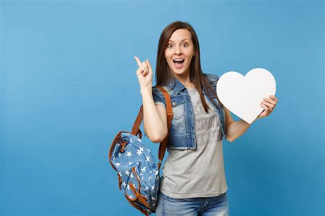 배낭에 복사 공간 포인팅 검지 손가락 옆으로 파란 배경에 고립으로 하얀 마음을 들고 젊은 놀된 여자 학생의 초상화 대학에서 교육입니다 광고에 대 한 공간을 복사 합니다 20