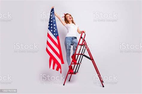 그녀의 전체 길이 몸 크기보기 그녀의 좋은 매력적인 쾌활한 쾌활한 흥분 행운의 소녀 는 밝은 흰색 파스텔 색상 배경 위에 고립 된 우리 플래그를 손에 들고 사다리에 서 T