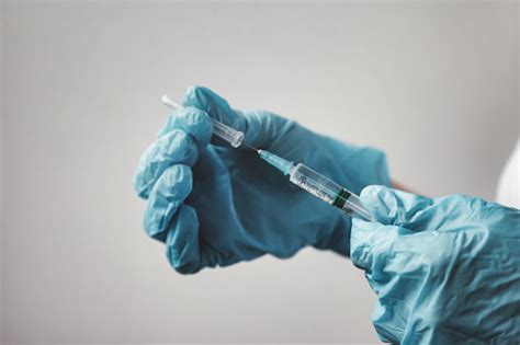 흰색 배경에 의료용 백신 주사 액체 약물 또는 마약이 있는 주사기로 파란색 라텍스 장갑을 낀 여성 의사의 손을 닫습니다 바늘