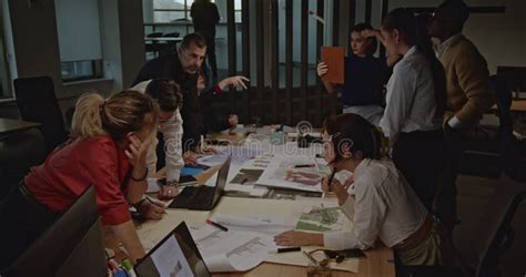 Diverse Business Team Collaborates On Project In Modern Office Reviewing Blueprints And