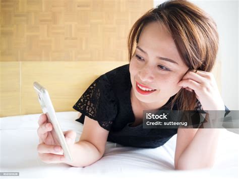 스마트폰 들고와 웃 고 보고 아시아 여 자가 침대에 누워 휴식과 행복 서핑 인터넷의 개념 30 39세에 대한 스톡 사진 및 기타