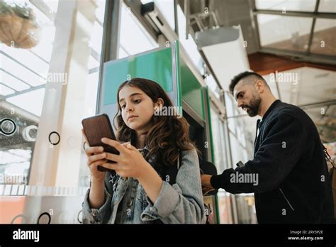 Girl Using Smart Phone With Father Accessing Atm Machine At Railroad