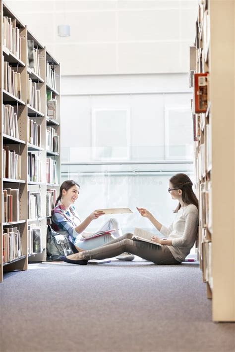 Students Passing Book While Sitting At University Library Stock Image