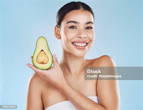 아름다운 젊은 혼합 인종 여성으로 스튜디오에서 파란색 배경에 고립 된 아보카도를 가지고 있습니다 그녀의 스킨 케어 정권은 그녀를 신선하게 유지합니다 빛나는 피부를 위해서는
