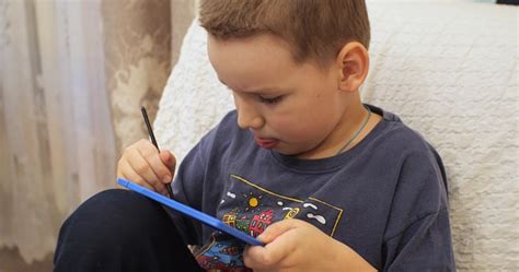 하얀 의자에 앉아있는 아이는 전자 태블릿에 그림을 그립니다 아이는 집에서 여가 시간을 보내며 그림을 그립니다 컨셉 어린이 아티스트는 전자 태블릿에 그림을 그립니다 가정