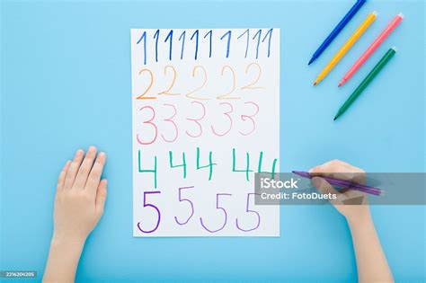 어린 아이 소년 손 색깔 펜을 들고 푸른 테이블 배경에 흰 종이에 다채로운 다른 숫자를 씁니다 파스텔 색상 학교 운동을합니다 근접 촬영 시점 촬영 하향식 보기 3에 대한