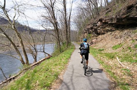 A Man Riding A Bike Down A Road Next To A River