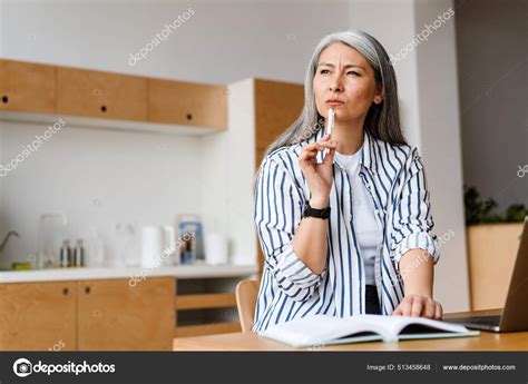 Serious White Haired Mature Woman Writing Notes Working Laptop Indoors