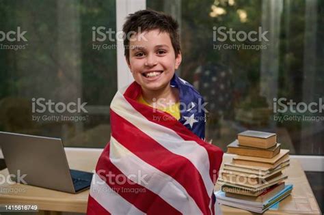 미국 국기에 싸인 사랑스러운 십대 여학생 노트북과 스택 워크북이있는 테이블 옆에 서서 카메라에 미소를 짓습니다 Stem 주제에 대한 스톡 사진 및 기타 이미지 Istock