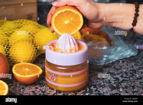 Woman squeezing orange with juicer or squeezer on the kitchen countertop background. No sugar or ...