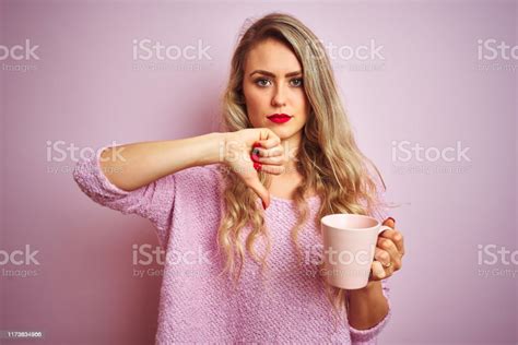화가 얼굴 엄지 손가락으로 싫어하는 것을 보여주는 부정적인 기호 거부 개념으로 분홍색 고립 된 배경 위에 커피 한 잔을 마시는