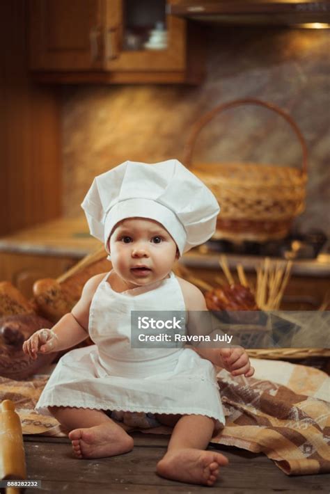 Niño Feliz En El Traje De Cocinero En La Cocina Sentado En La Mesa Entre Cestas Con Sabrosos