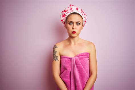 재미 있는 얼굴과 분홍색 고립 된 배경 퍼핑 뺨을 통해 샤워 후 수건과 목욕 모자를 입고 젊은 아름다운 여자 공기 미친 표정으로 입이 팽창 수건에 싸다에 대한 스톡 사진 및