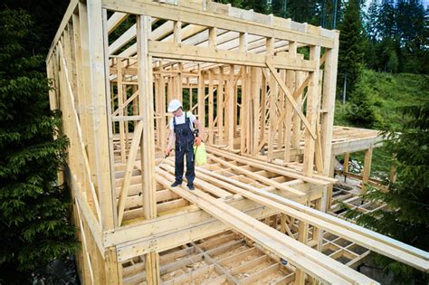 Worker Applying Fire Retardant Using Sprayer While Constructing Wooden Frame House Near Forest