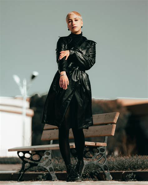 Young Brunette Woman In Black Pvc Matrix Style Trench Coat Posing At A