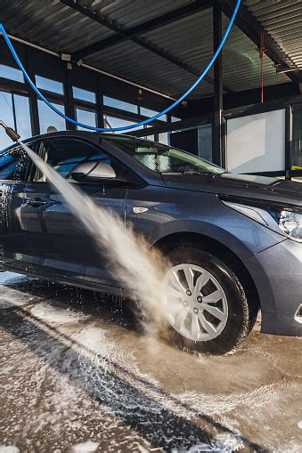 한 남자가 가압 된 물로 호스를 사용하여 셀프 서비스 세차장에서 차의 바퀴를 씻습니다 세차장에 대한 스톡 사진 및 기타 이미지