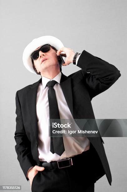 양복을 입은 성공한 사업가는 흰색 모자와 선글라스를 입고 스마트폰으로 이야기하며 하얀 배경을 올려다본다 성공으로 가는 길에 비즈니스 라이프 결심에 대한 스톡 사진 및 기타