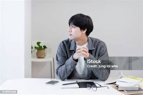 실내 책상에 앉아 창밖을 내다보며 여가 시간을 즐기는 젊은 남자 대학생의 꿈결 같은 초상화 남자에 대한 스톡 사진 및 기타