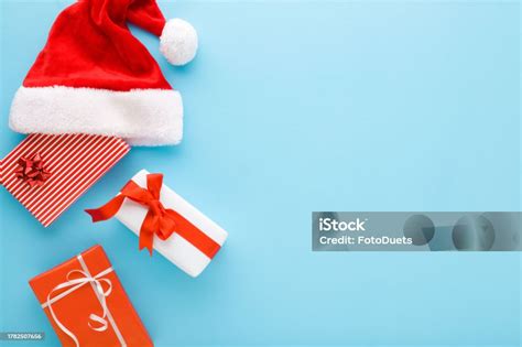 밝은 파란색 테이블 배경에 흰색 모피와 화려한 포장 선물 상자를 가진 밝은 빨간 모자 파스텔 색상 근접 촬영 크리스마스나 새해에 선물을 드립니다 하향식 보기 텍스트를 위한