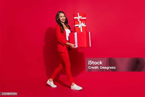 귀여운 갈색 머리 아가씨의 전체 크기 프로필 사진 선물 홀드 착용 양복 스니커즈 붉은 색 배경에 고립 25 29세에 대한 스톡 사진 및 기타 이미지 Istock