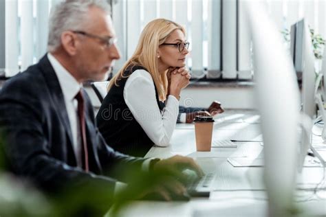 Focus Of Blonde Businesswoman Looking At Computer Monitor Near Multicultural Coworkers In Office