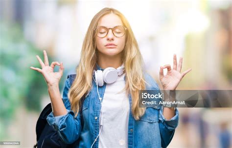 격리 된 배경 위에 헤드폰 및 안경 착용 해 젊은 아름 다운 금발 학생 여자 휴식과 명상 손가락으로 제스처를 하 고 폐쇄 눈으로 웃 고 요가 개념 대학생에 대한 스톡 사진