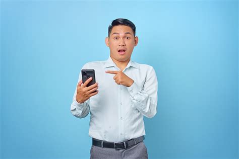 파란 배경에 스마트 폰에 손가락을 가리키는 충격 젊은 잘 생긴 사업가 30 34세에 대한 스톡 사진 및 기타 이미지 30 34세 Brand Name Smart