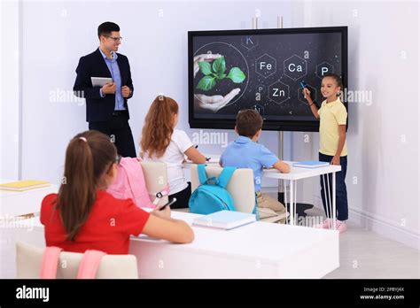 Teacher And Pupil Using Interactive Board In Classroom During Lesson