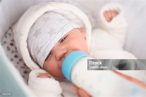 어머니는 밝은 파란색 젖꼭지가 있는 플라스틱 병에서 아기 소년 유아 아이 우유를 먹이부모의 손으로 백인 백인 아이가 눈에 보이는흰색 시트로 아기 캐리지에 누워 2명에 대한