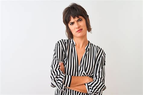 고립 된 흰색 배경 회의론자 및 긴장 위에 서있는 줄무늬 셔츠를 입은 젊은 아름다운 여성은 교차 된 팔로 얼굴에 표정을