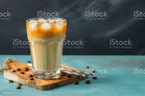 크림을 뿌린 높은 유리에 아이스 커피를 쏟아붓고 가벼운 돌 배경에 커피 콩을 뿌립니다 튜브가있는 추운 여름 음료 복사 공간 0