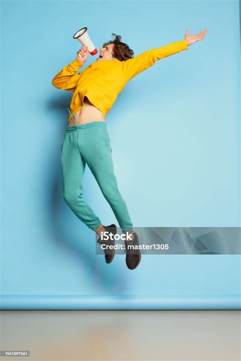 곱슬머리를 한 젊은 남자의 초상화 파란색 배경 위에 고립된 점프에서 확성기로 외치는 모습 휴대용 마이크에 대한 스톡 사진 및 기타 이미지 휴대용 마이크 남자 스튜디오