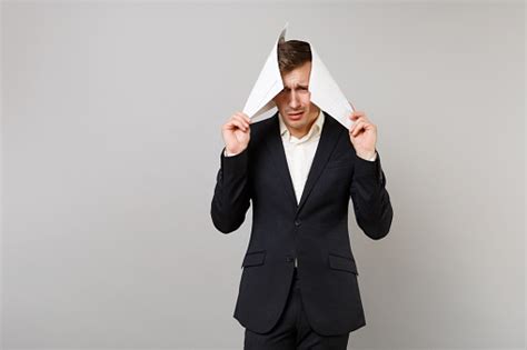 스튜디오에서 회색 벽 배경에 고립 된 머리에 종이 문서를 들고 클래식 블랙 정장 셔츠에 불만족 젊은 비즈니스 남자 업적 경력 자산 사업 개념 복사 공간을 모의 합니다 검은