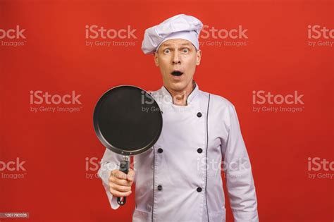 빨간 벽 배경 위에 고립 된 프라이팬을 들고 웃는 요리 유니폼에서 즐거운 수석 남자의 이미지 개념에 대한 스톡 사진 및 기타 이미지 Istock