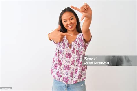 편안한 꽃무늬 티셔츠를 입은 젊은 중국 여성이 행복한 얼굴로 손과 손가락으로 프레임을 만드는 고립 된 흰색 배경 위에 서