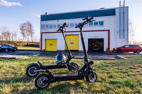 야외에서 두 개의 검은색 전기 스쿠터 사진 건물 근처의 푸른 잔디밭에서 킥스쿠터를 타세요 갑판에 보호 헬멧 생태 교통 개념 사진