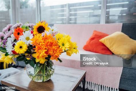 소파 소파와 밝은 쿠션이 있는 현대적인 아늑한 조명 온실실을 배경으로 커피 테이블에 거대한 여러 가지 색상의 다양한 혼합 꽃 꽃다발이 있는 꽃병 인테리어에 신선한 꽃입니다