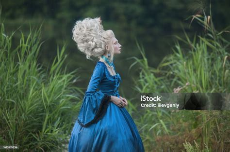 호수 배경에 금발 머리를 가진 르네상스 공주 뷰티 메이크업 자연에 헤어 스타일로 배를 가진 동화 속 로코코 여왕 파란색 드레스의 모델 다리에 역사적인 헤어 스타일을 가진
