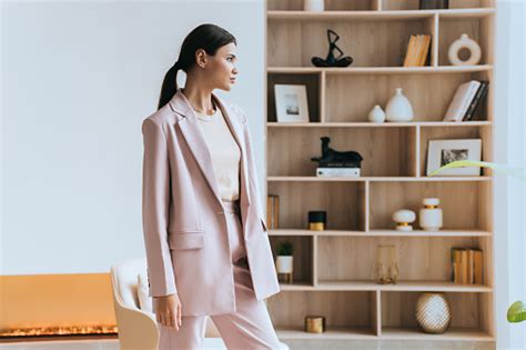 밝은 분홍색 정장을 입고 거실에 서 있는 예쁜 패션 모델 매력적인 아시아 젊은 성인 여성이 멀리 보고 있다 화려한 우아한 한국 소녀는 경력에 대해 생각합니다 사업가 여자에