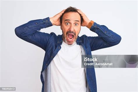 중년 잘생긴 남자 를 입고 파란색 데님 셔츠 위에 서 고립 된 흰색 배경 미친 머리에 손을 무서워 두려워하 고 오픈 입으로 충격의 놀라움 남자에 대한 스톡 사진 및 기타
