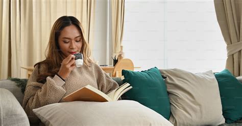 평화로운 아시아 여자가 책을 읽고 소파에서 커피를 마시고 있다 사진 Unsplash의 아늑한 이미지