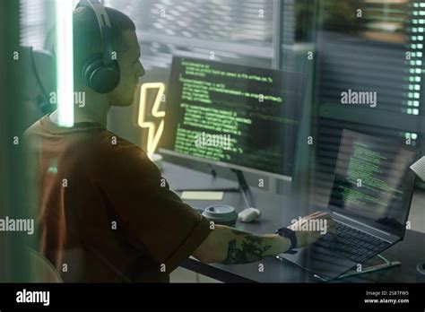 Shot Through Glass Wall Of Male Senior Developer In Headphones Coding