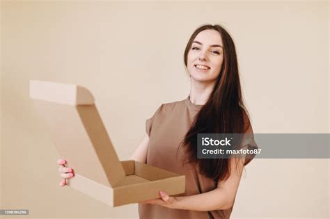 젊은 예쁜 여자는 손에 빈 골판지 상자를 들고 서서 베이지 색 배경으로 카메라를 바라 봅니다 감정에 대한 스톡 사진 및 기타 이미지 Istock