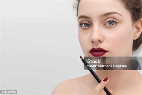 파란 눈과 짙은 빨간색 립스틱이 메이크업 브러시를 들고 있는 아름다운 젊은 여성의 사진을 클로즈업합니다 왼쪽에 공간을 복사합니다 Maroon Lipstick에 대한 스톡